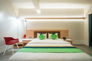 Quarto de hotel com uma cama grande, cabeceira de madeira, escrivaninha com cadeira e telefone.