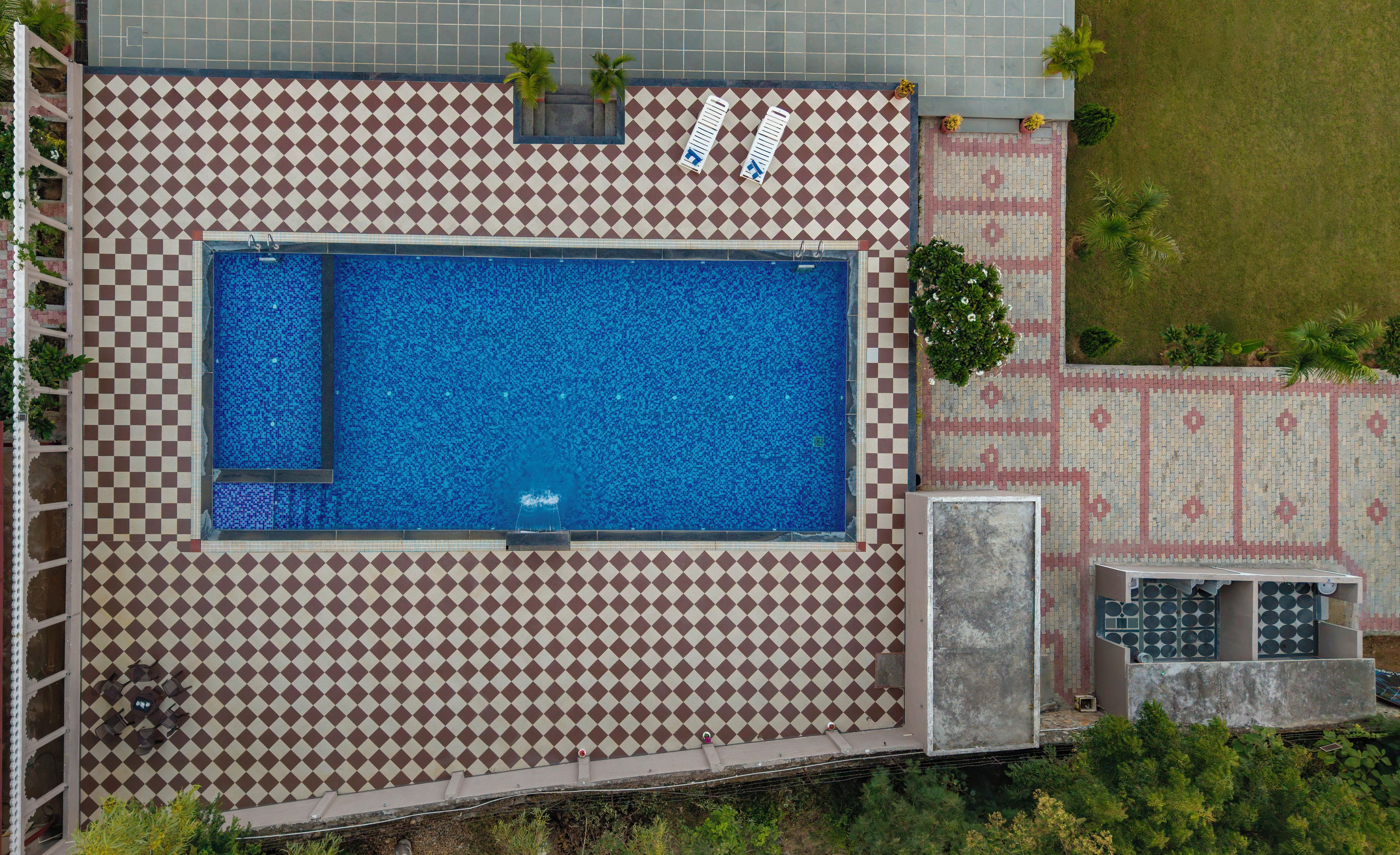 Piscina no terraço com padrão de ladrilhos xadrez, rodeada por vegetação e um muro decorado.
