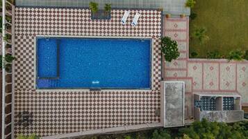 Piscina no terraço com padrão de ladrilhos xadrez, rodeada por vegetação e um muro decorado.