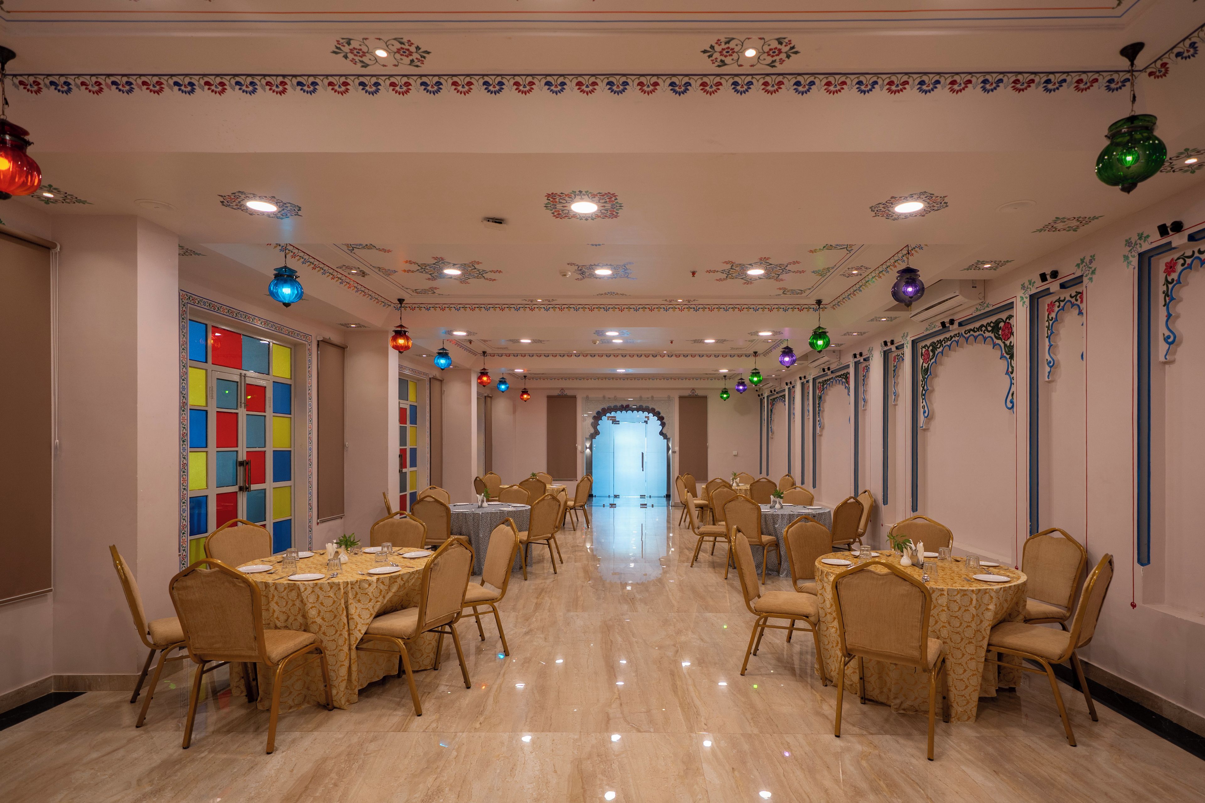 Um espaço de refeições de hotel com mesas e cadeiras redondas, uma parede colorida e luminárias decorativas no teto.