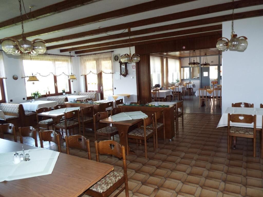 Uma sala de jantar com mesas e cadeiras de madeira, piso ladrilhado e luminárias pendentes.