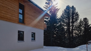 Um edifício moderno com fachada de madeira e parede branca, rodeado por neve e árvores altas.