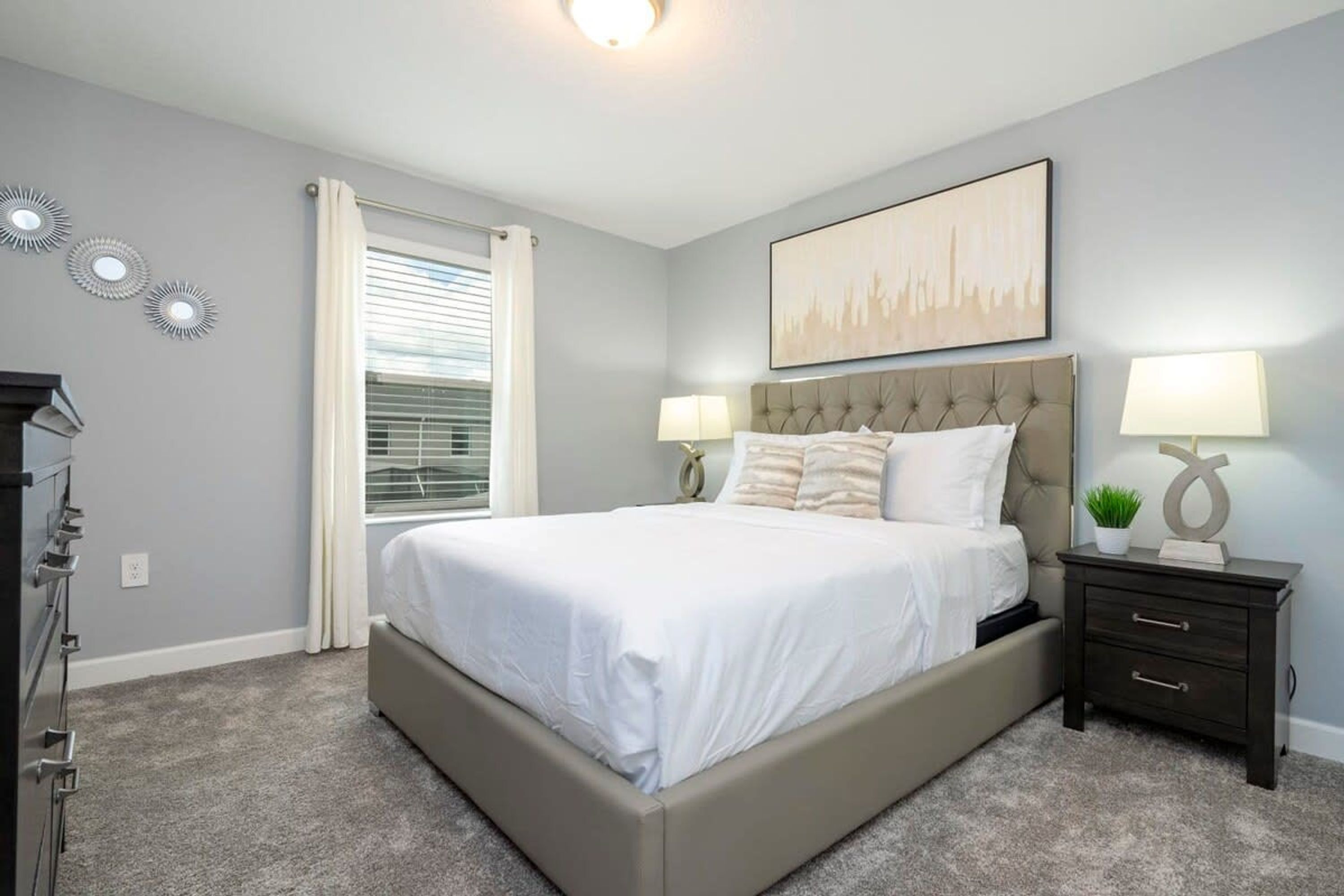 Quarto com uma cama grande, duas mesas de cabeceira com abajures, cômoda e janela com cortinas.