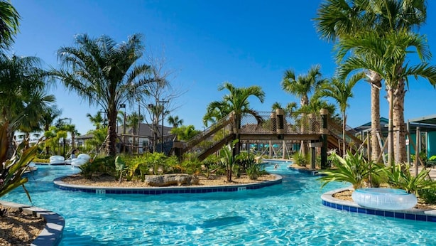 Área de piscina com palmeiras, um escorregador e um edifício ao fundo.