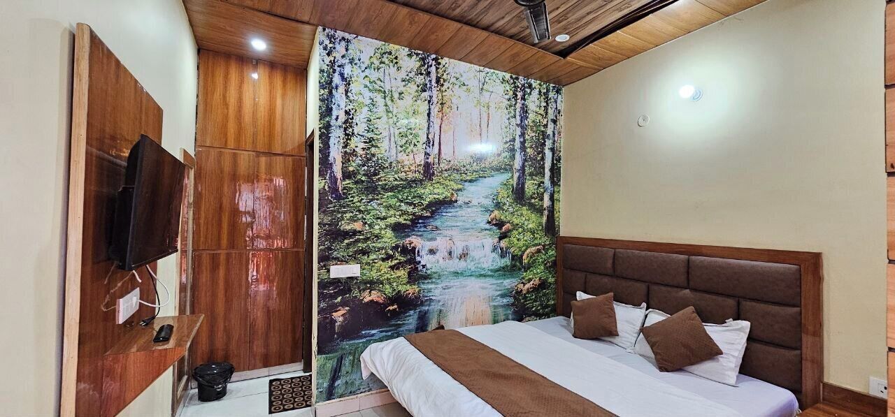 Quarto com uma cama, uma televisão fixada em um painel de madeira e um mural temático de floresta.