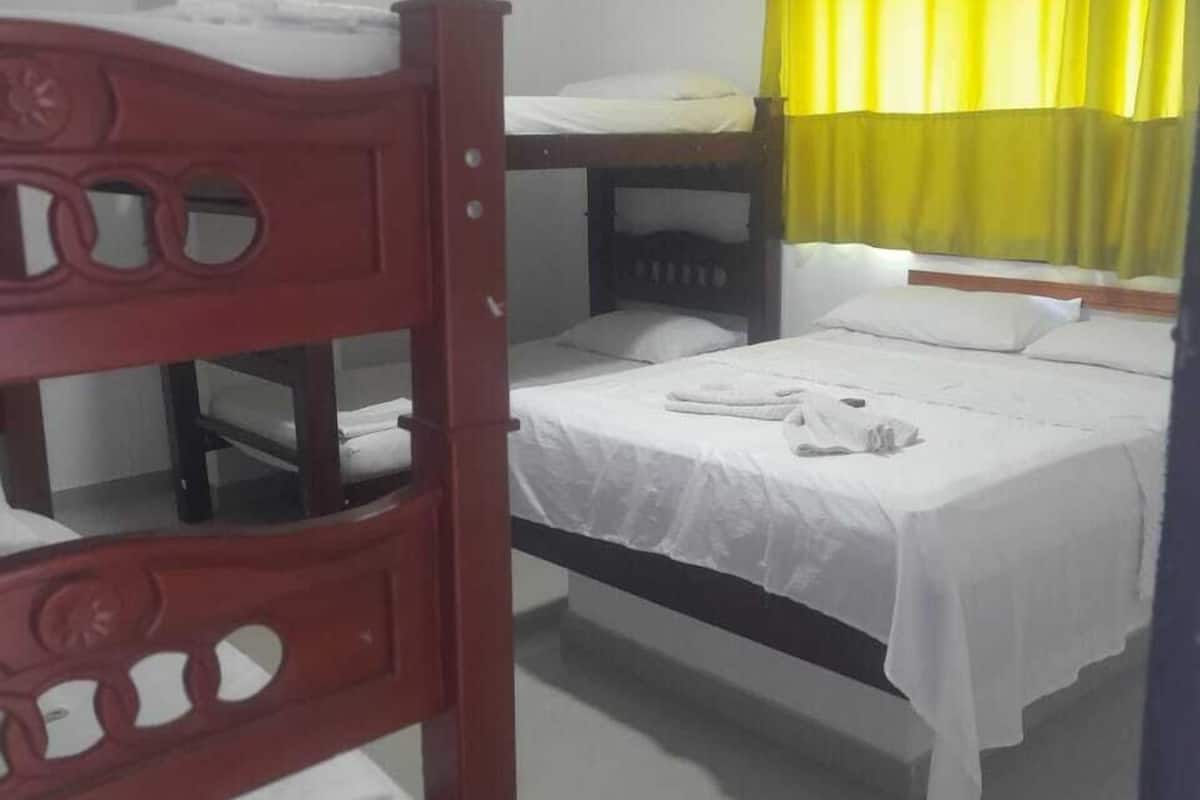 Um quarto de dormitório com beliches, uma cama, uma janela com cortinas amarelas e uma parede branca.