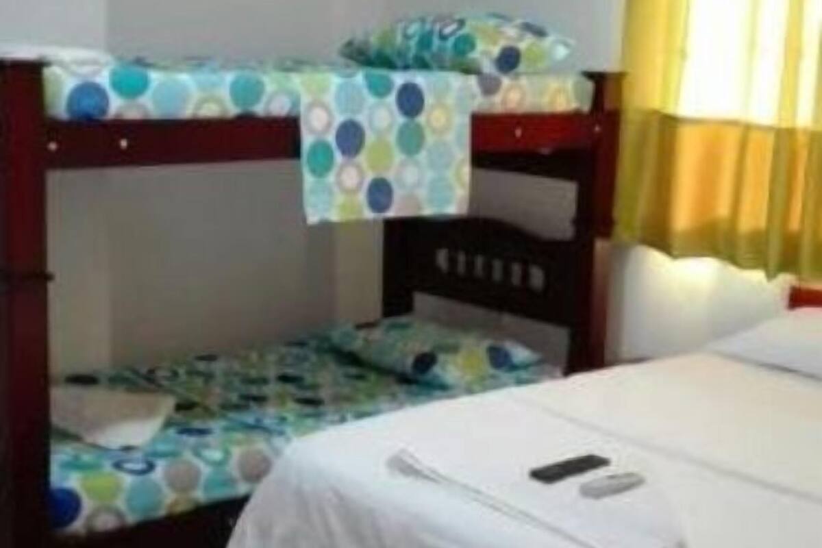 Quarto com beliches, uma cama de solteiro, um tapete pequeno e uma janela com cortinas.