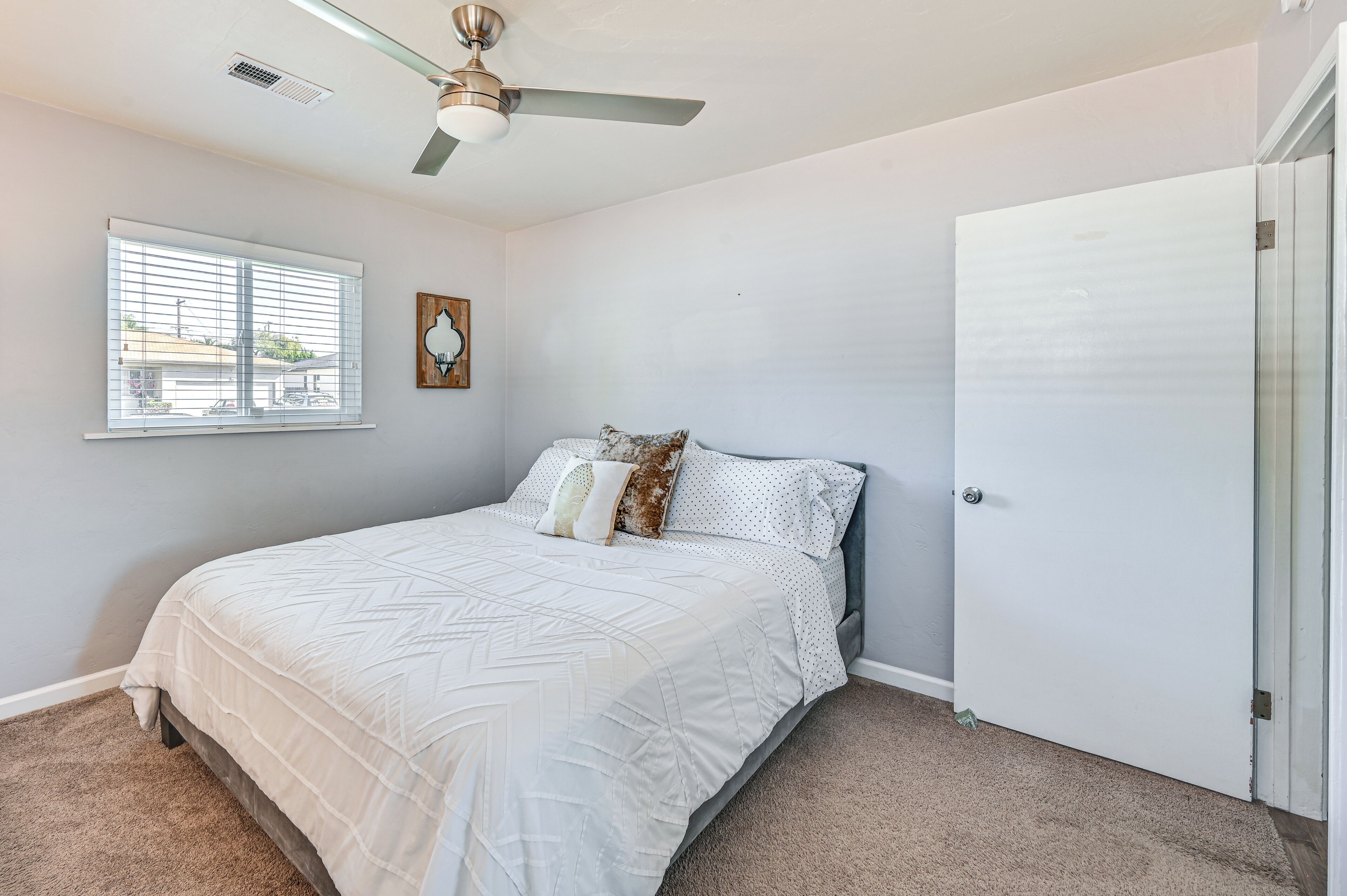 Um quarto com cama, ventilador de teto, janela com persianas e porta.