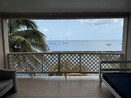 Uma varanda com vista para o mar, uma cama branca e um sofá cinzento.