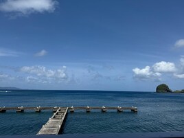 Um píer se estende por águas azuis calmas, com um céu claro e uma pequena ilha ao longe.