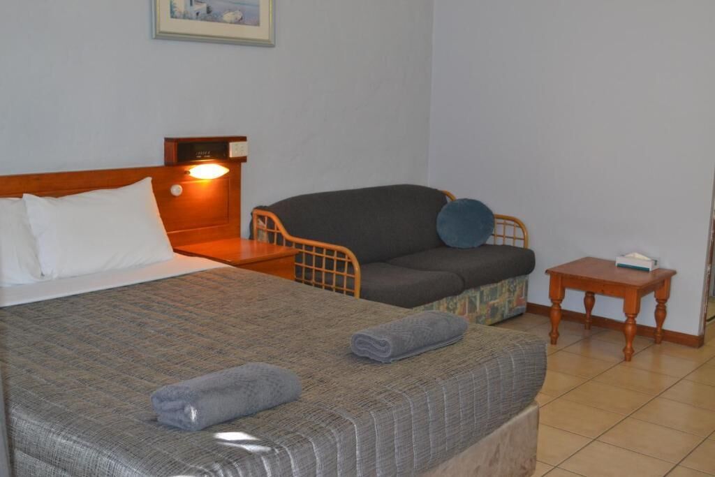 Quarto de hotel com cama, sofá, mesa de cabeceira e uma pequena mesa.