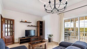 Sala de estar com televisão, sofá, mesa de centro e lustre.