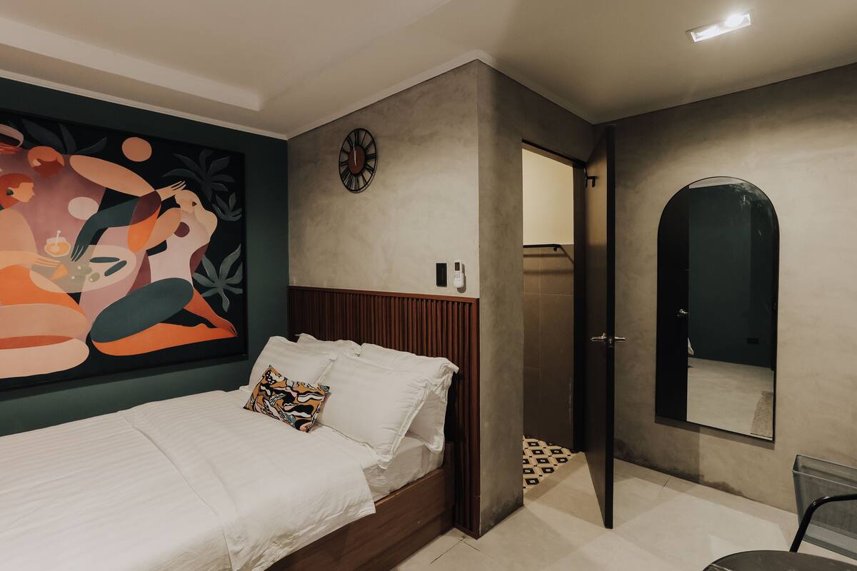 Quarto moderno com cama, uma pintura abstrata grande, relógio e espelho.
