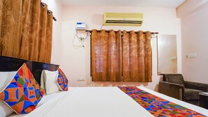 Quarto de hotel com cama, escrivaninha, cadeira, janela com cortinas, ar condicionado e tomada na parede.