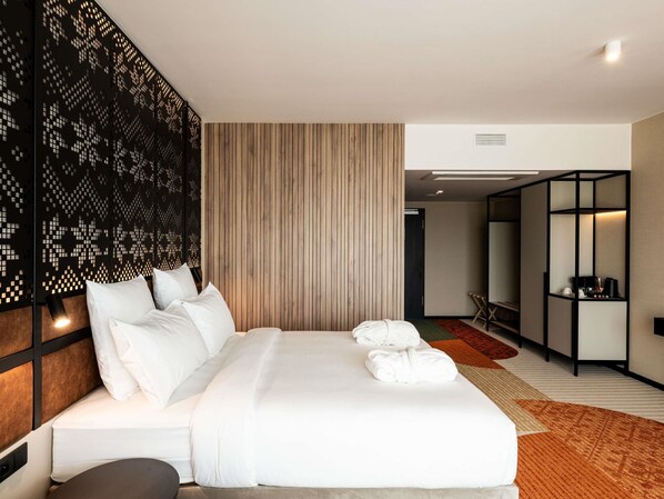 Quarto de hotel moderno com uma cama grande, parede de painéis de madeira e um painel decorativo preto, além de um pequeno espaço de estar.