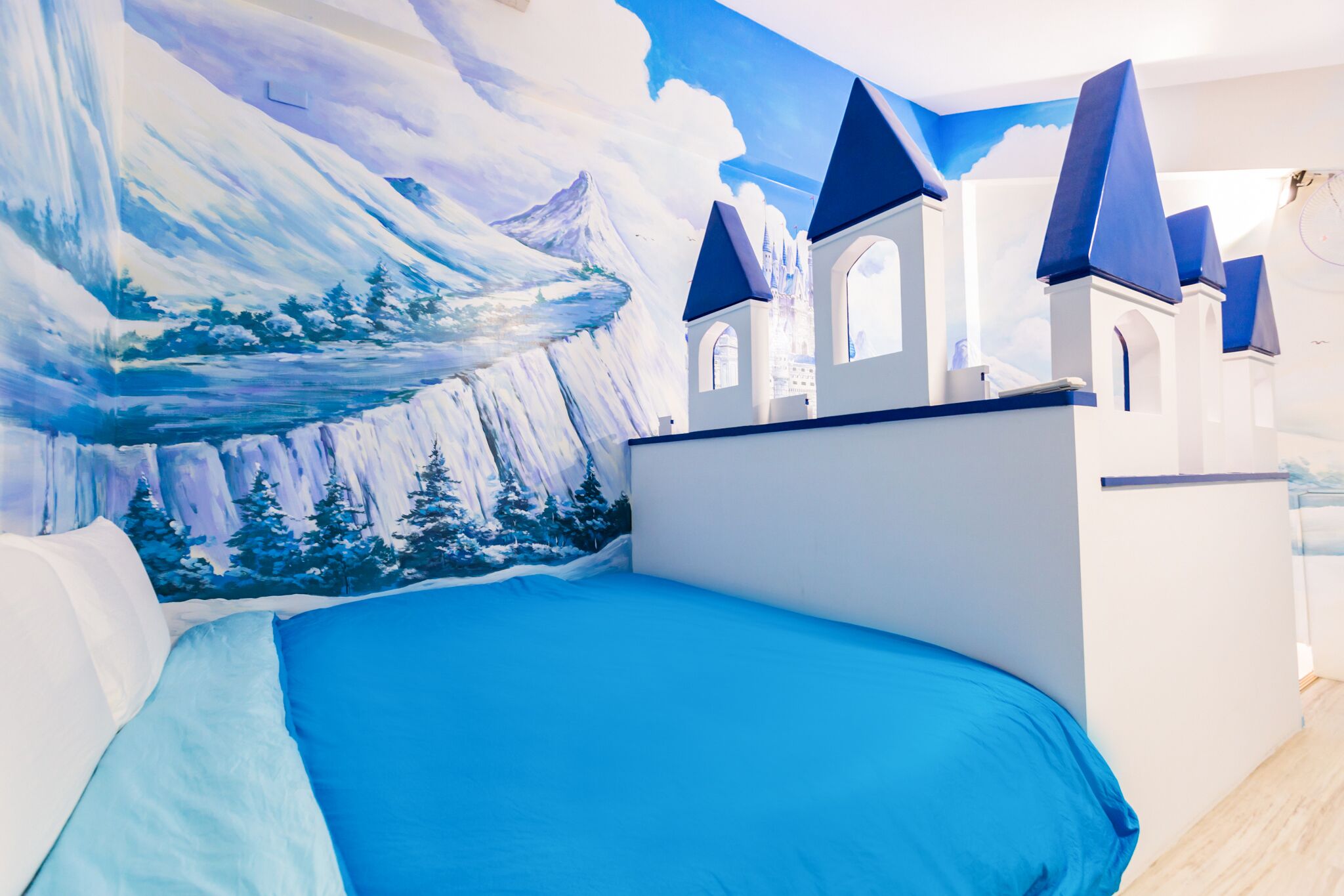 Quarto com cama, um mural de paisagem montanhosa e uma estrutura que lembra um castelo.