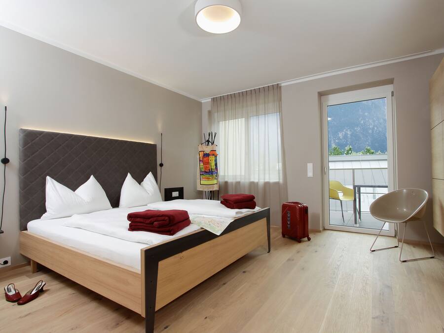 Quarto de hotel moderno com uma cama, uma cadeira, uma mala e uma varanda com vista.
