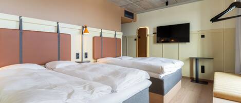 Quarto de hotel com duas camas, uma televisão e uma mesa pequena.
