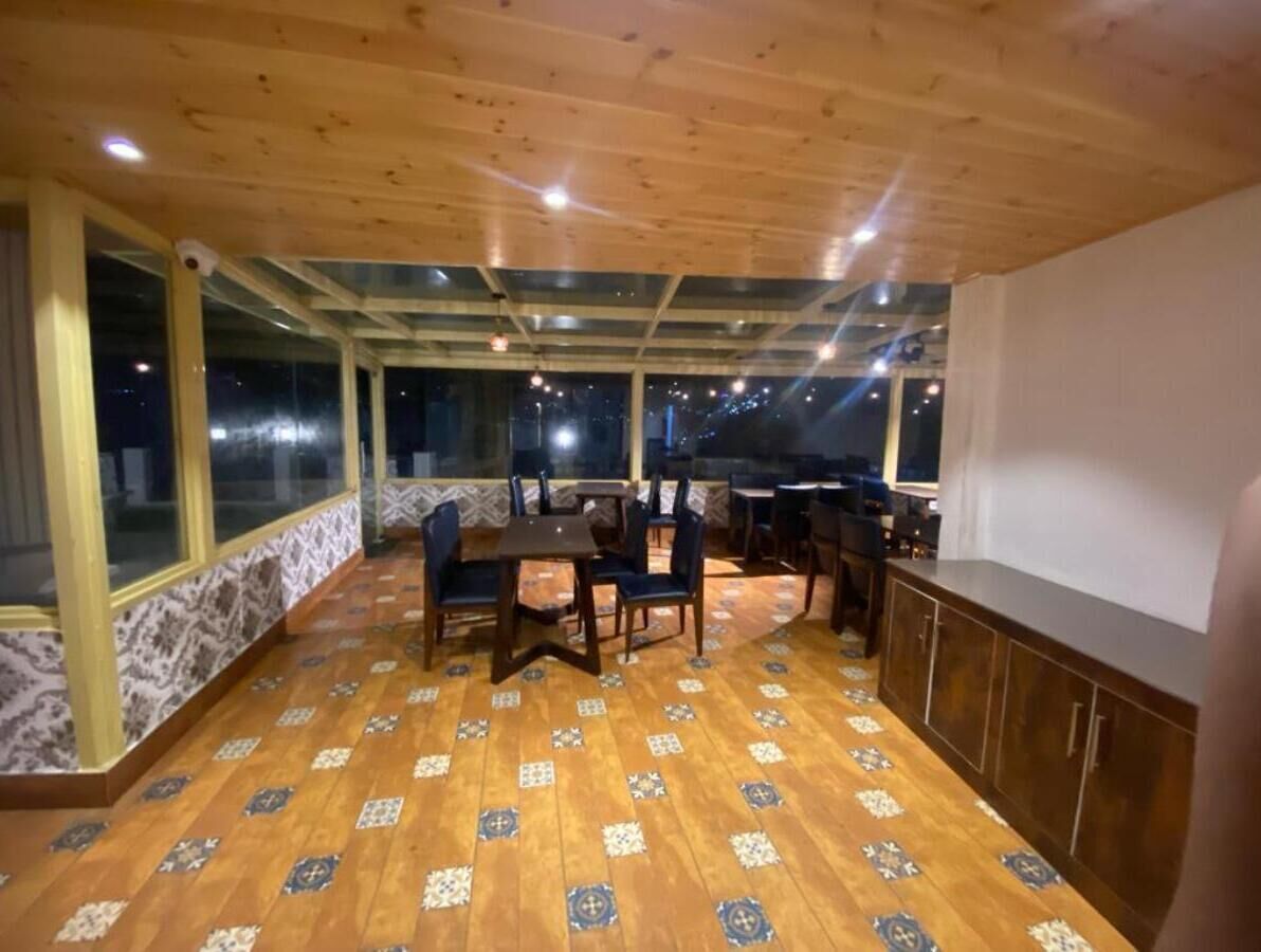 Uma área de refeições com piso de madeira, uma mesa com cadeiras e vista através de grandes janelas.