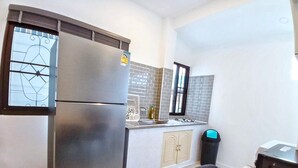 Uma cozinha compacta com geladeira de aço inoxidável, fogão a gás e pia. Há duas cadeiras e uma mesa pequena com toalha de mesa xadrez.