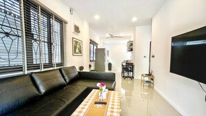 Uma sala de estar moderna com um sofá de couro preto, uma mesa quadriculada e uma grande televisão de tela plana.