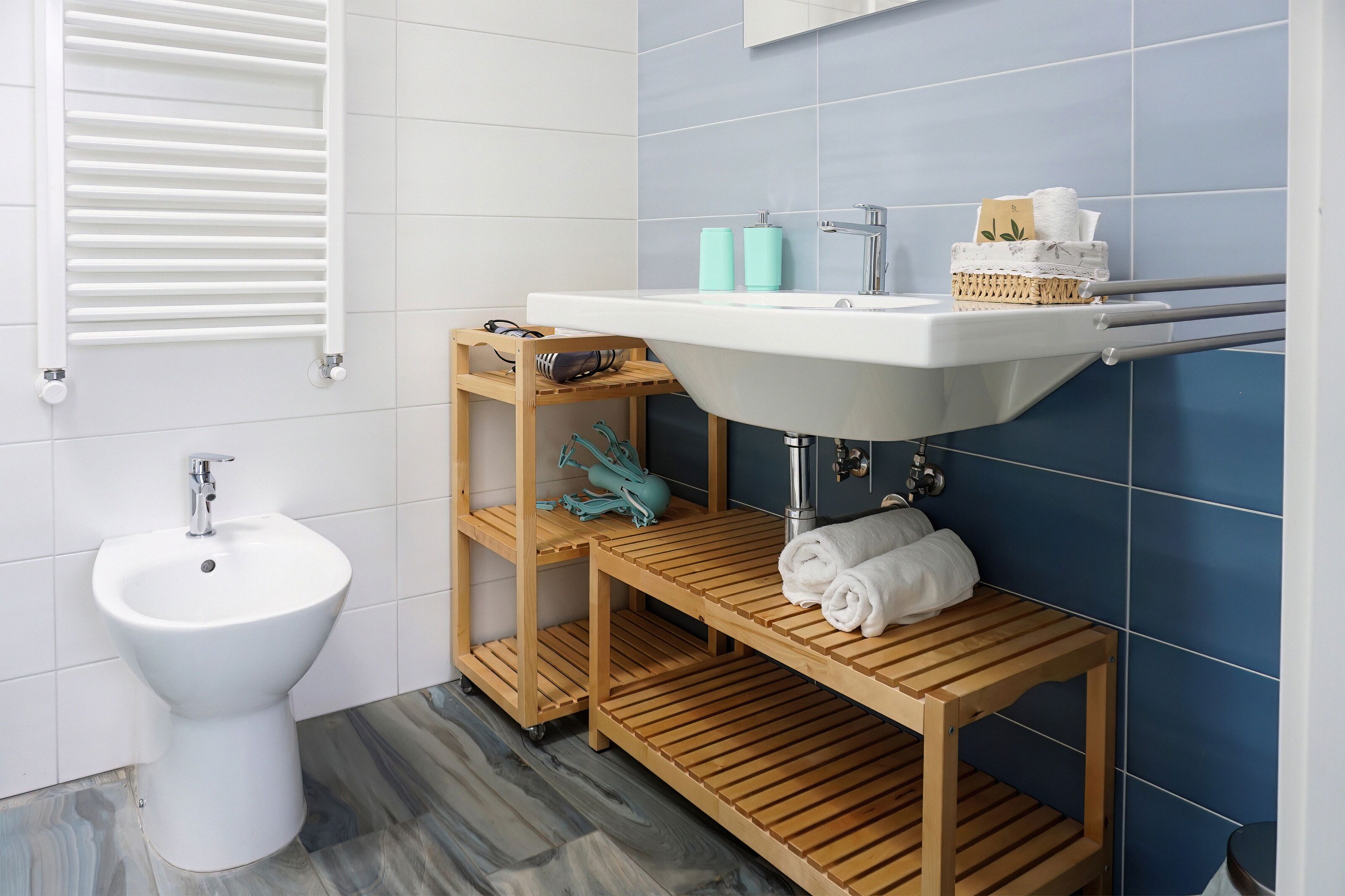 Um banheiro moderno com um bidê pedestal branco, um armário de vaidade de madeira com pia e uma parede revestida de azulejos azuis.