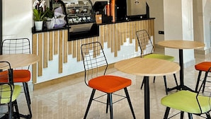 Um café moderno com balcão de madeira, espaço para baristas e diversas áreas de estar com cadeiras coloridas.