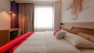 Quarto de hotel com uma cama, uma mesa e uma cadeira.