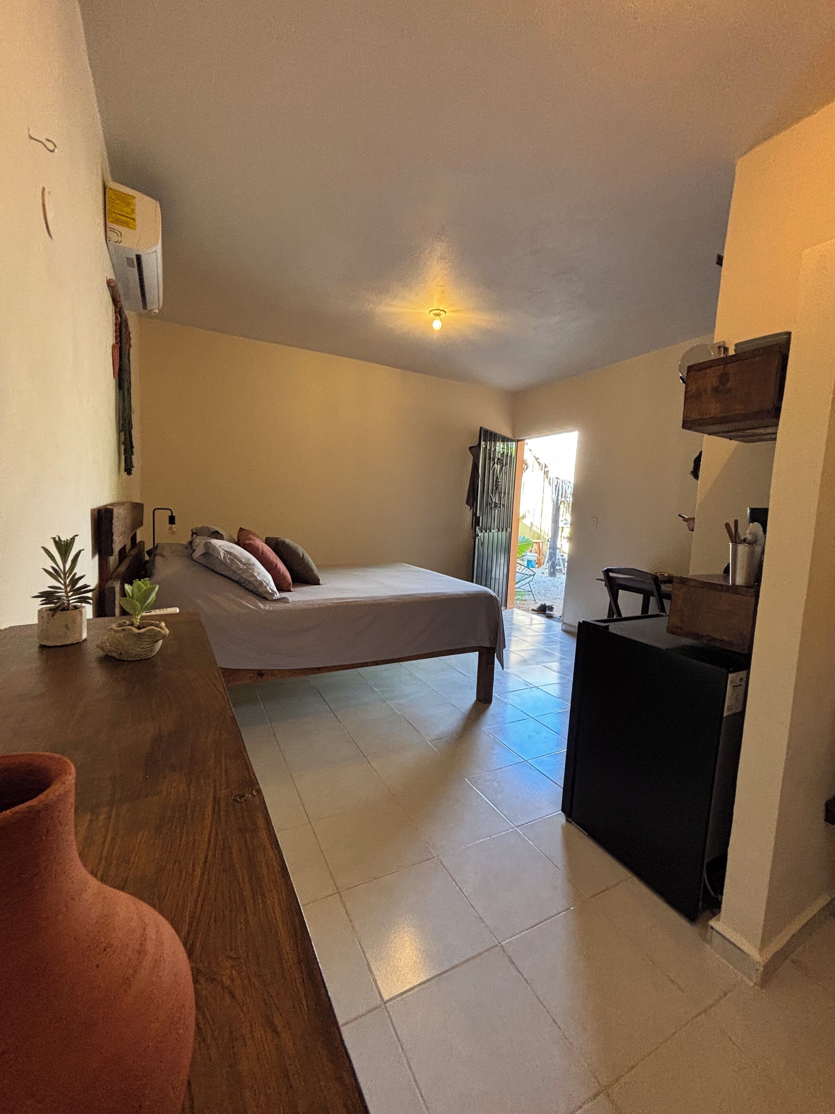Quarto com cama, escrivaninha e cómoda. Há uma janela com cortinas e vista para o exterior.