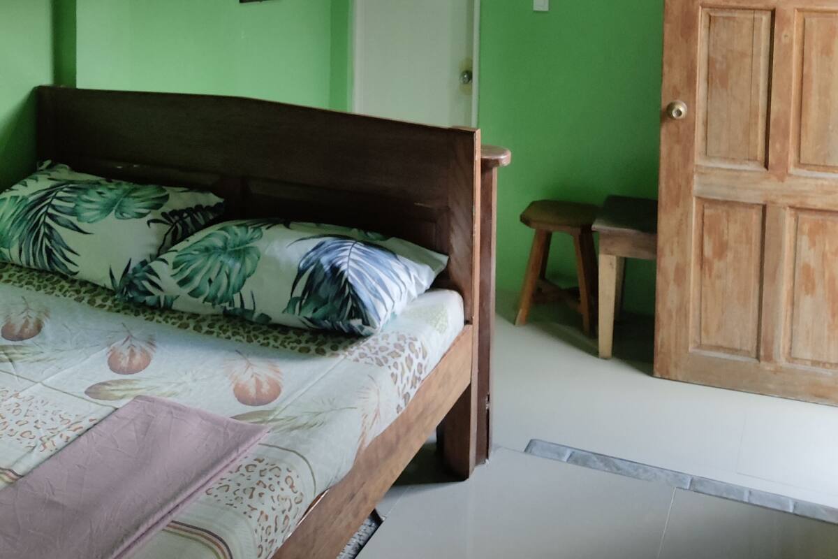Quarto com cama, porta de madeira e um pequeno banquinho.