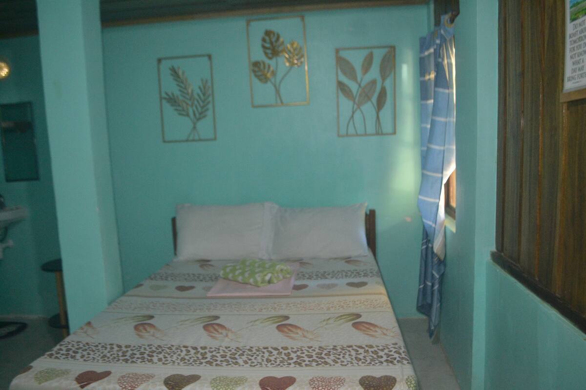 Quarto com cama, almofadas, manta e decoração nas paredes.