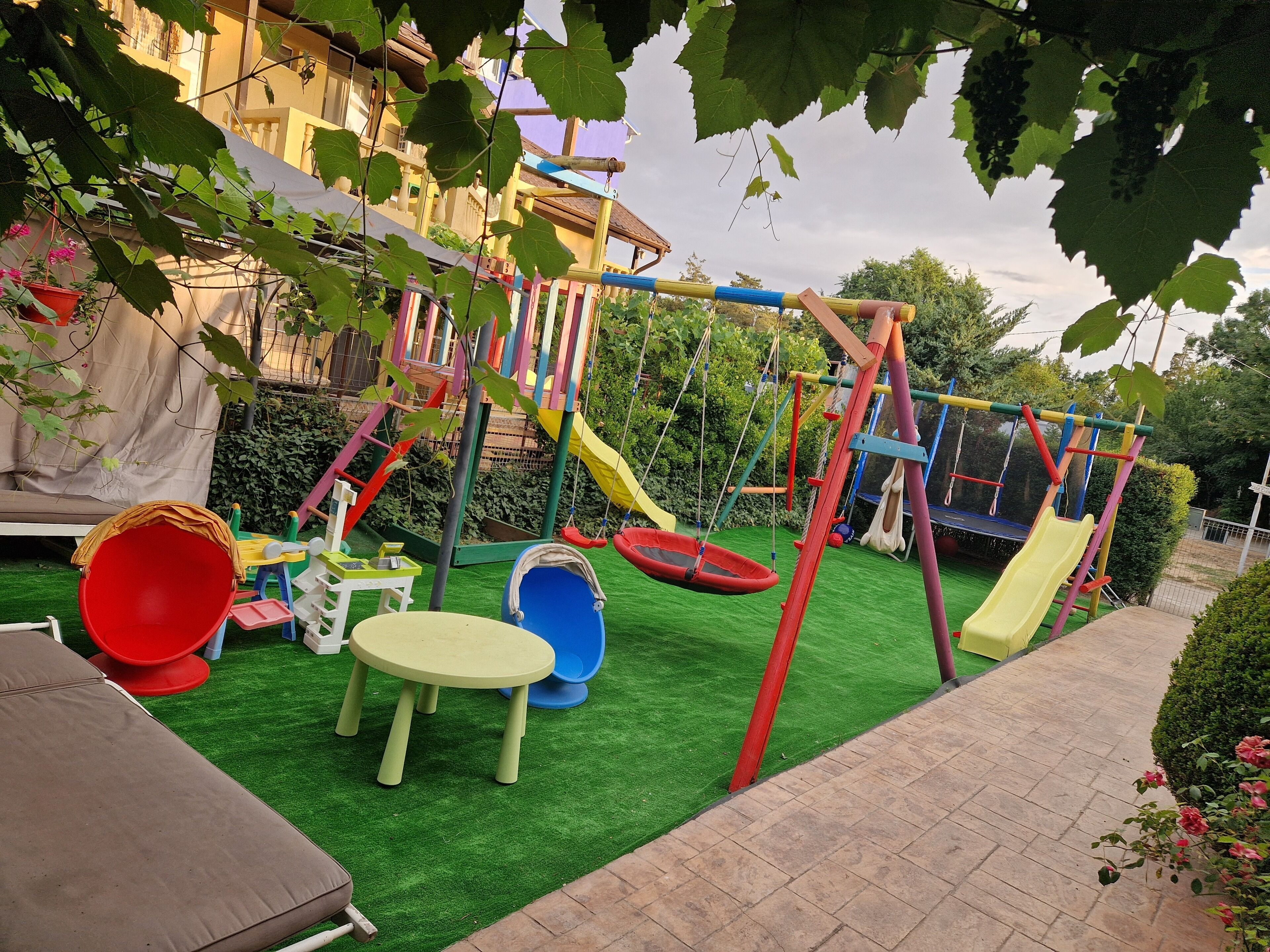 Uma área de recreação infantil com escorrega, baloiços e uma mesa pequena.