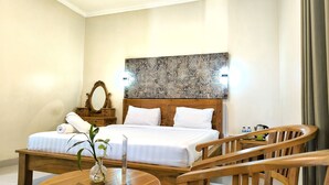 Quarto de hotel com uma cama de madeira, uma mesa de cabeceira com um vaso, uma cadeira e um espelho fixado na parede.