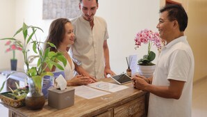 Uma receção com balcão de madeira, plantas em vasos, caixa de tecidos e um tablet.