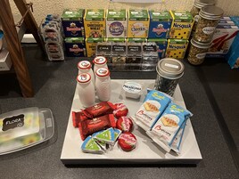 Uma bancada de cozinha com diversos alimentos e recipientes, incluindo caixas de cereais, potes de frutos secos e embalagens de lanches.