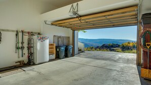 Garagem com piso de concreto, ventilador de teto e vista para montanhas através de uma porta aberta.