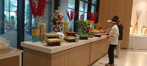 Espaço de buffet com diversas opções de comida e decoração, incluindo um pinheiro de Natal.