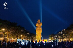 Uma multidão se reuniu em volta de uma grande escultura iluminada à noite.