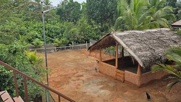 Uma cabana rústica com telhado de palha, cercada por uma área vedada com chão de terra.