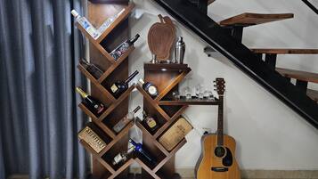 Uma estante de madeira para vinhos com várias prateleiras, um violão e uma escadaria ao fundo.