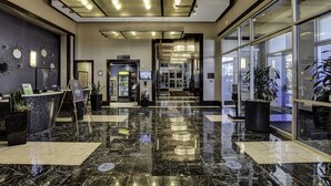 Um saguão de hotel com piso de mármore, balcão de recepção e porta de vidro que dá para a entrada.