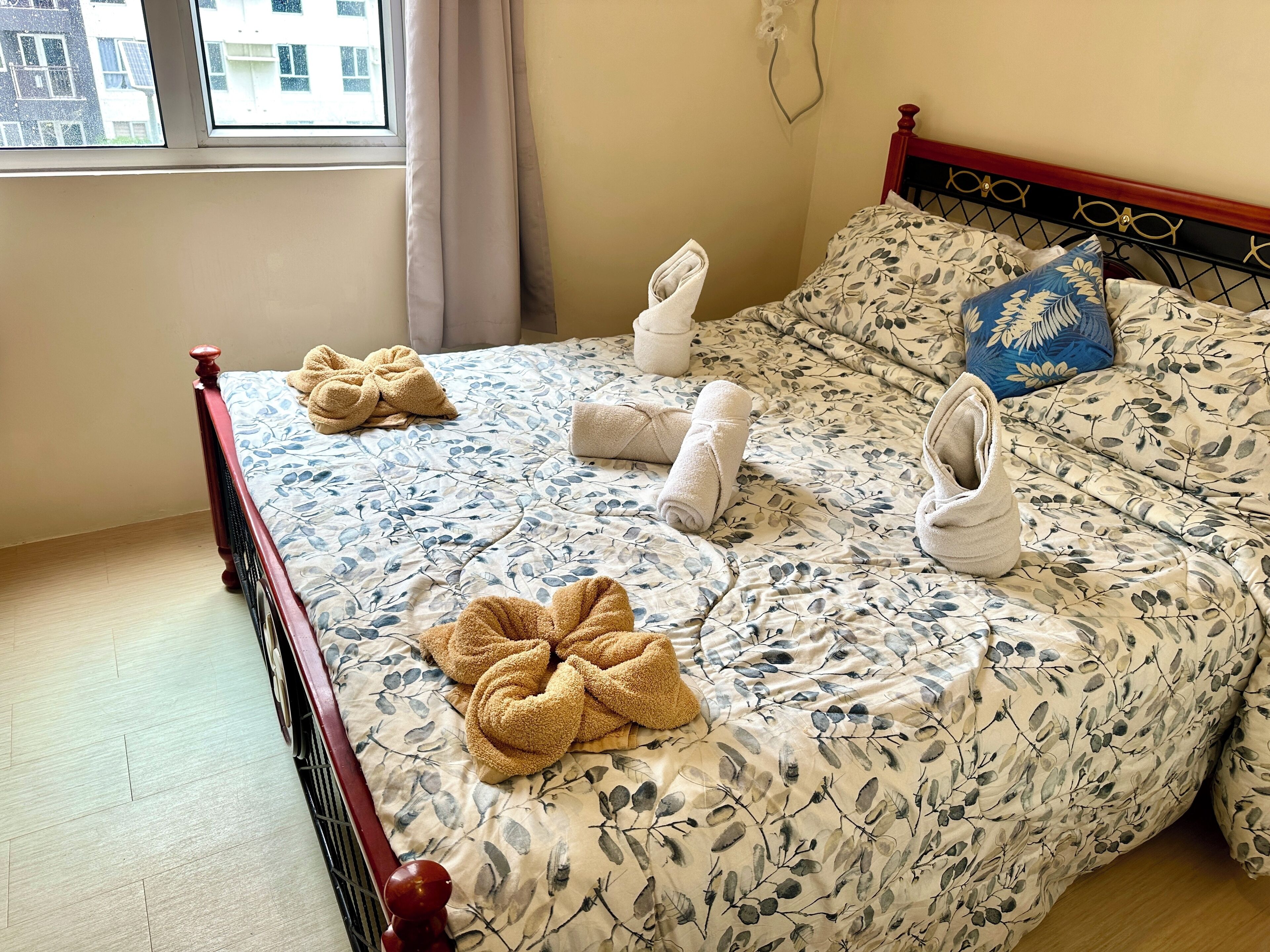 Uma cama bem arrumada com roupa de cama florida, cabeceira de madeira e vista para edifícios lá fora.