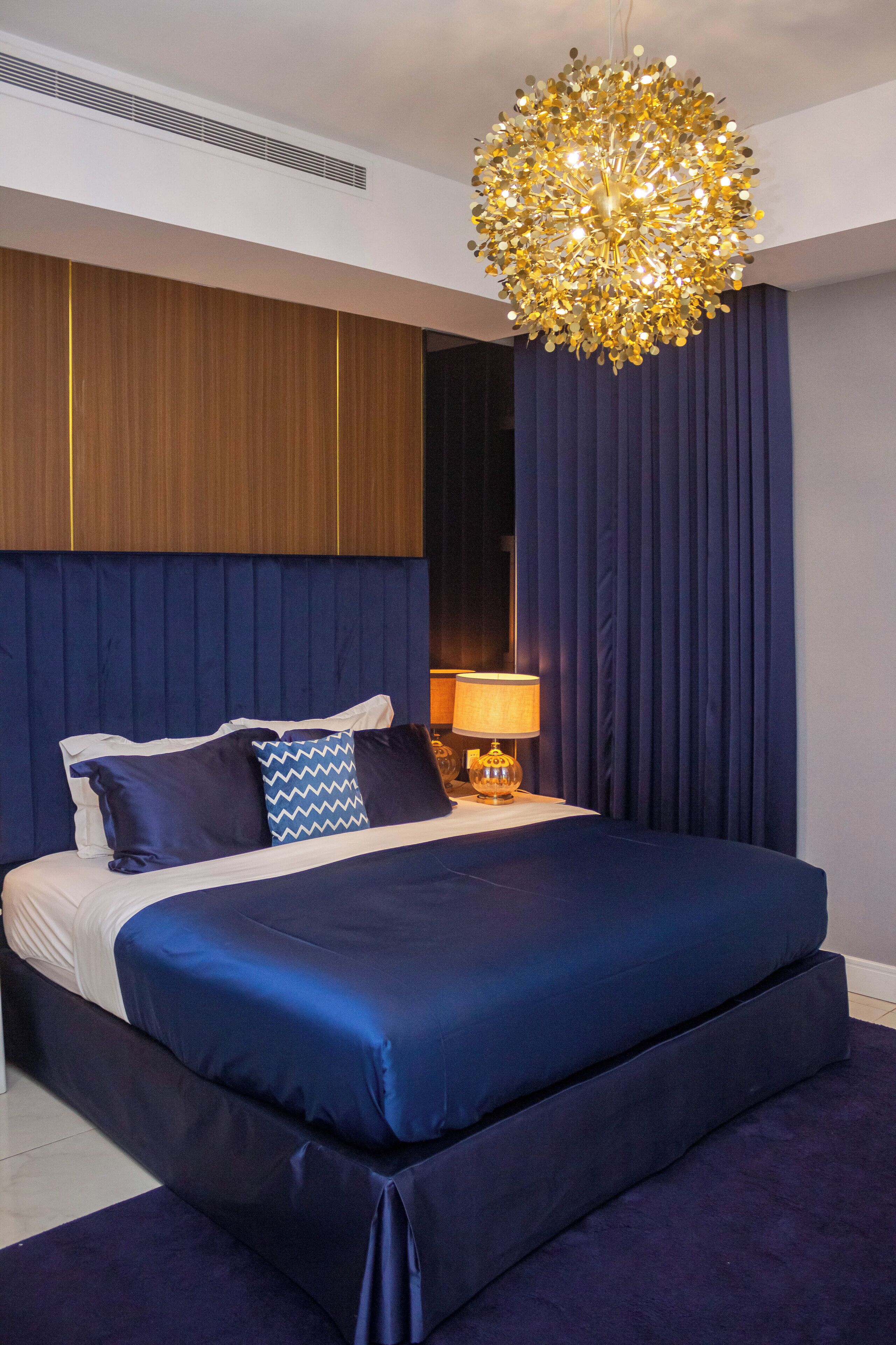 Quarto moderno com uma cama grande, um lustre decorativo e uma mesa de cabeceira com abajur.