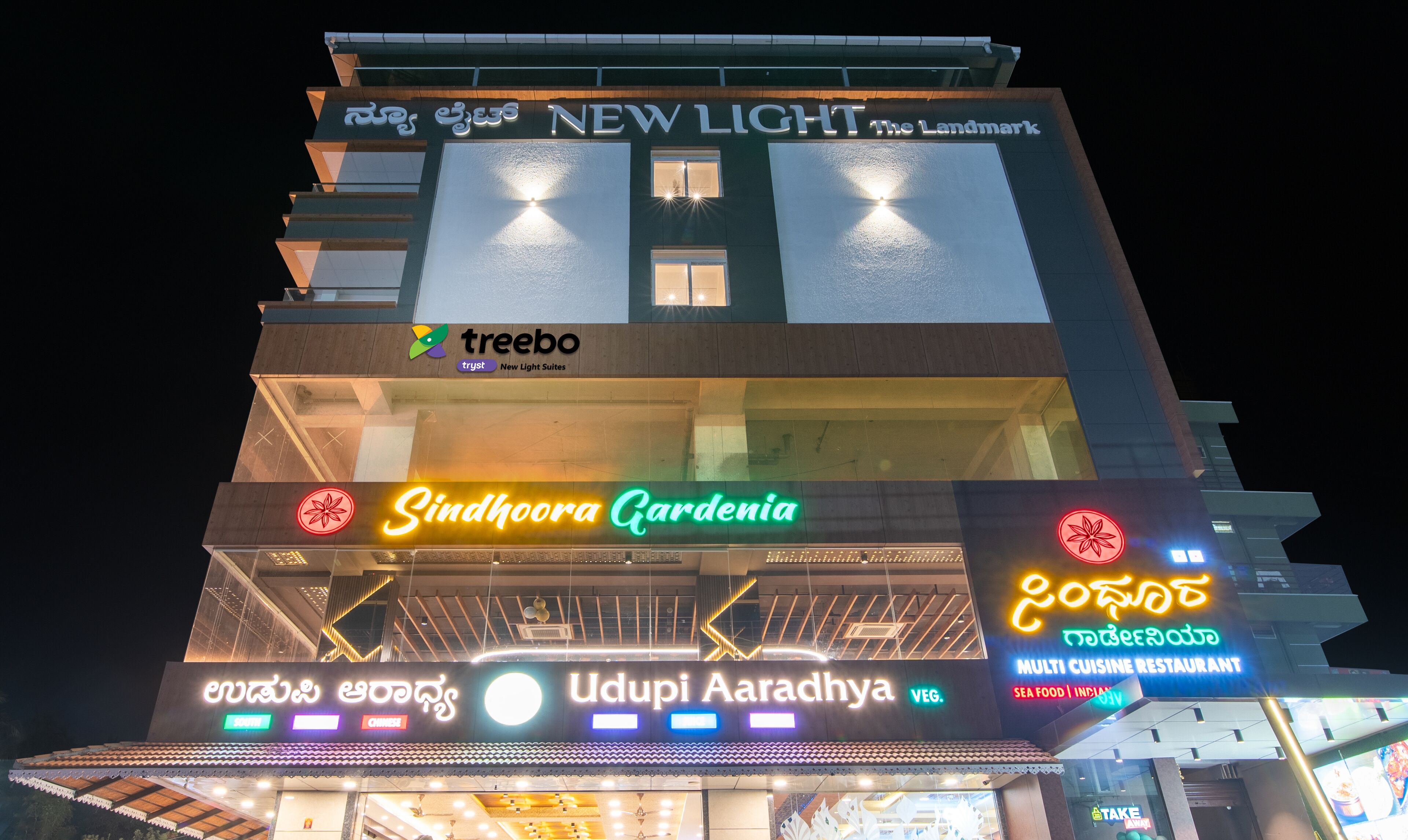 Um edifício com vários andares e diversos letreiros de restaurantes, incluindo 'Sindhura Gardenia' e 'Udupi Aarachya'.