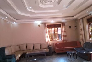 Uma sala de estar com um sofá bege, um sofá vermelho, uma poltrona azul e uma mesa de centro de vidro.