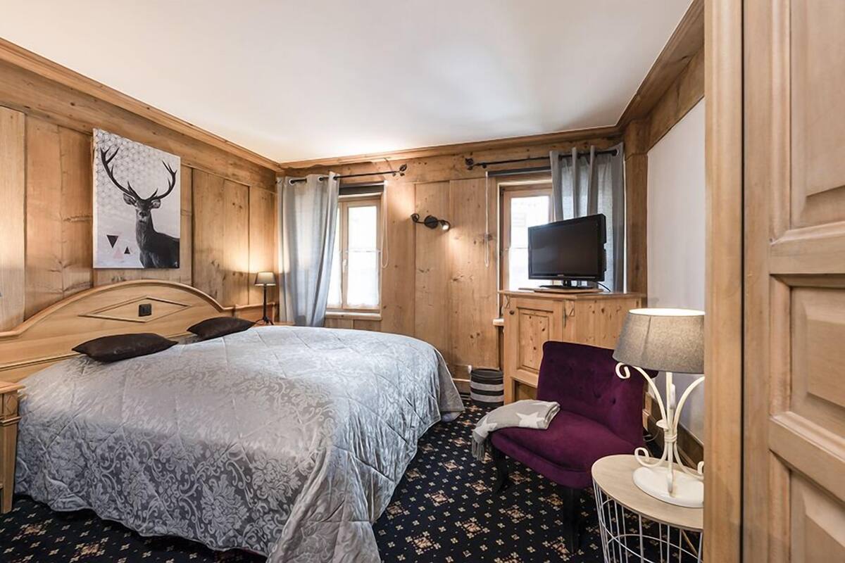 Quarto de madeira com uma cama, uma televisão, uma cadeira e um abajur.