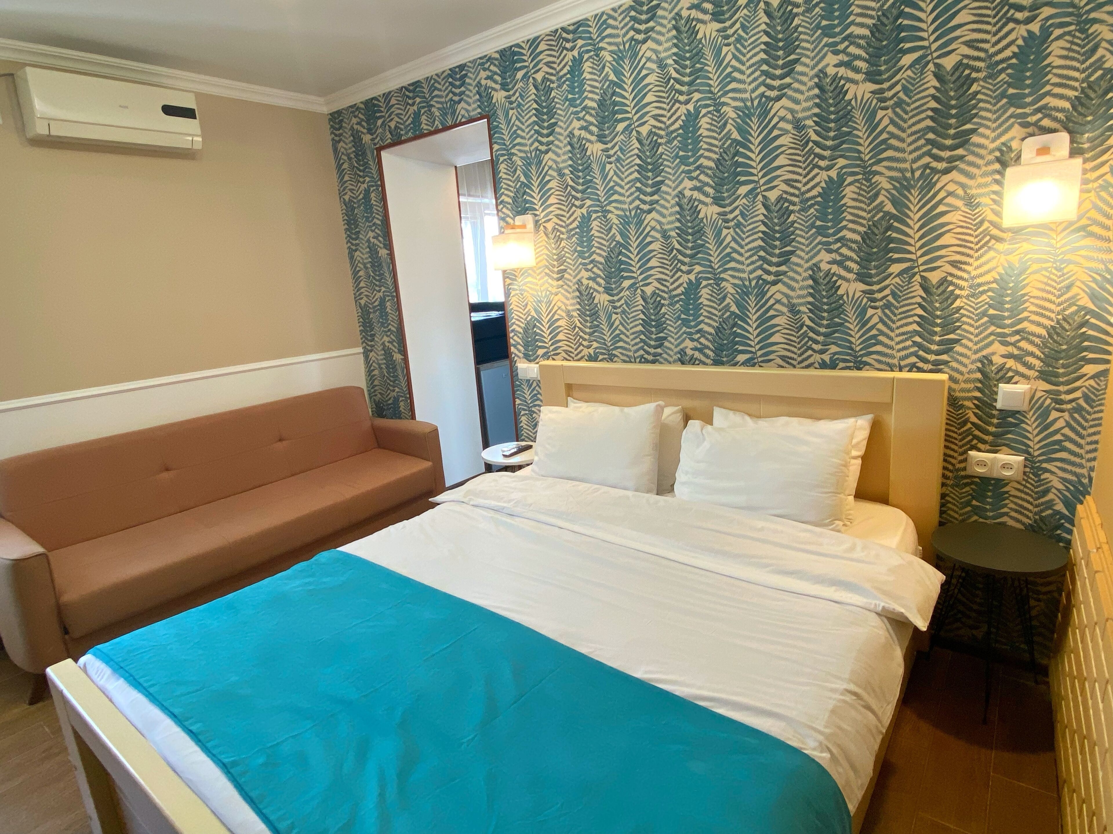 Quarto de hotel com uma cama, um sofá, um espelho e uma parede com padrão de folha.