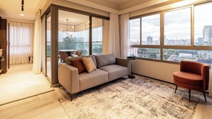 Uma sala de estar moderna com sofá, poltrona e uma janela ampla com vista para a cidade.