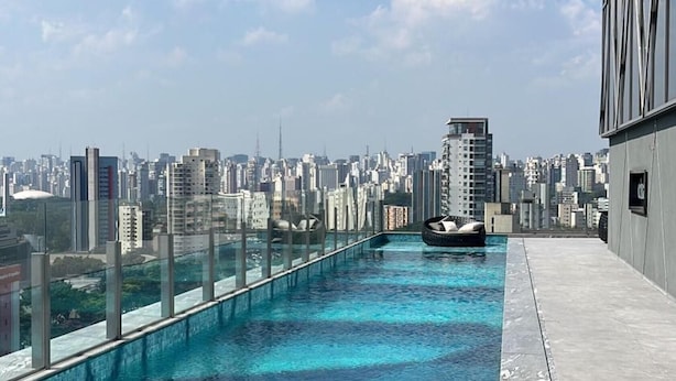 Piscina no terraço com vista para a cidade, água azul cristalina e um edifício moderno com fachada de vidro.