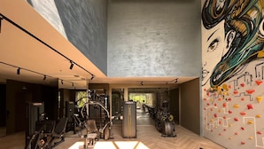 Uma academia com equipamentos de exercício, um grande mural e teto alto.